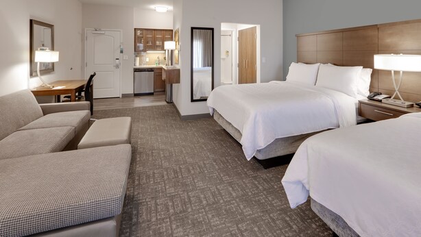Quarto de hotel com uma cama grande, um sofá, uma escrivaninha e uma cozinha compacta.