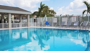 Piscina azul límpida com cerca branca, cadeiras de descanso e área coberta com telhado.