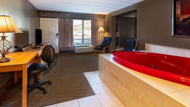 Quarto de hotel com escrivaninha, cadeira de escritório, uma banheira vermelha grande e uma televisão.