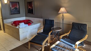 Quarto de hotel com uma banheira vermelha, duas poltronas azul-escuro, uma mesa redonda pequena e um abajur.