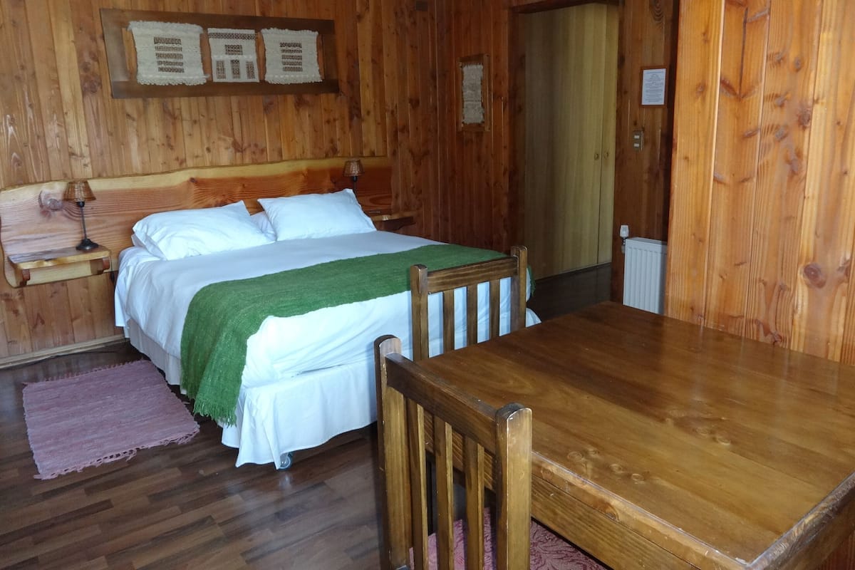 Quarto de madeira com cama, mesa e cadeira. Inclui cabeceira de madeira, mesa de cabeceira e porta.