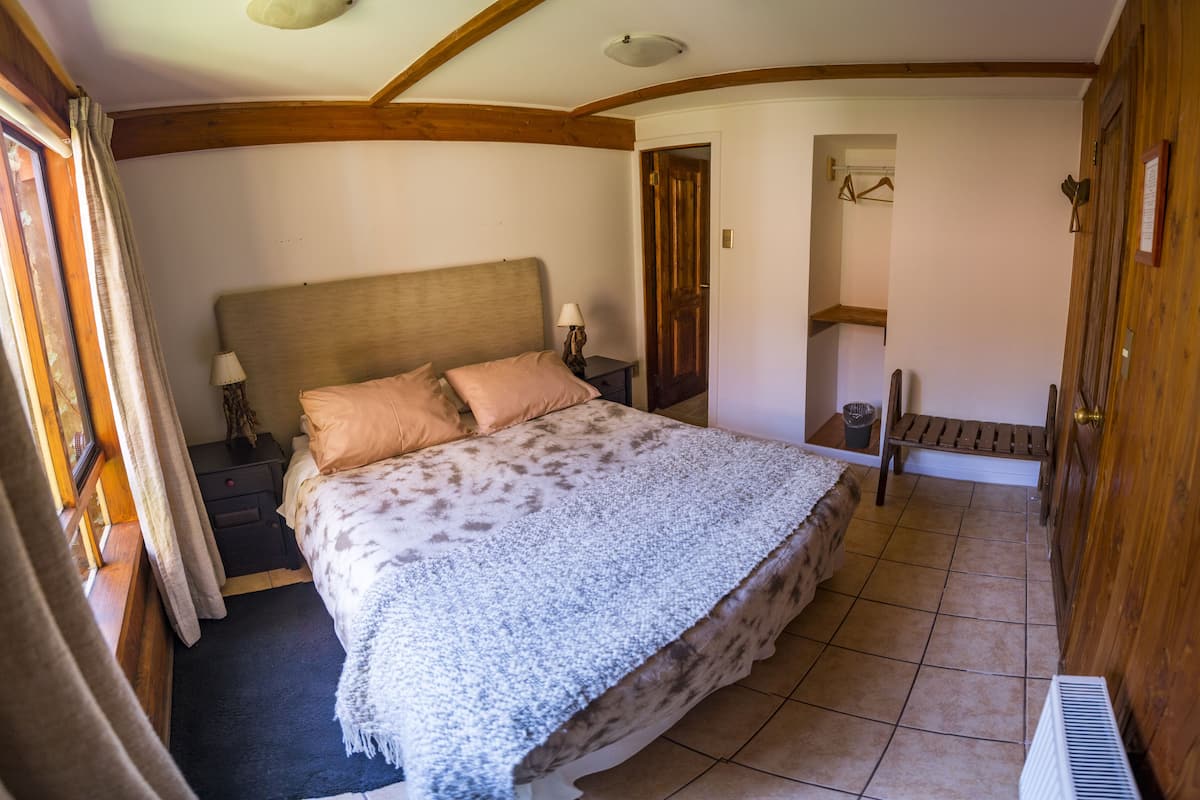 Quarto com cama, mesa de cabeceira, luminária, banco e radiador.