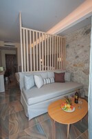 Uma sala de estar moderna com sofá, divisória de madeira, parede de pedra e mesa de jantar com frutas e vinho.