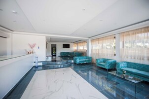 Uma sala de estar ampla com piso de mármore, sofás verde-água e uma mesa de centro de vidro.