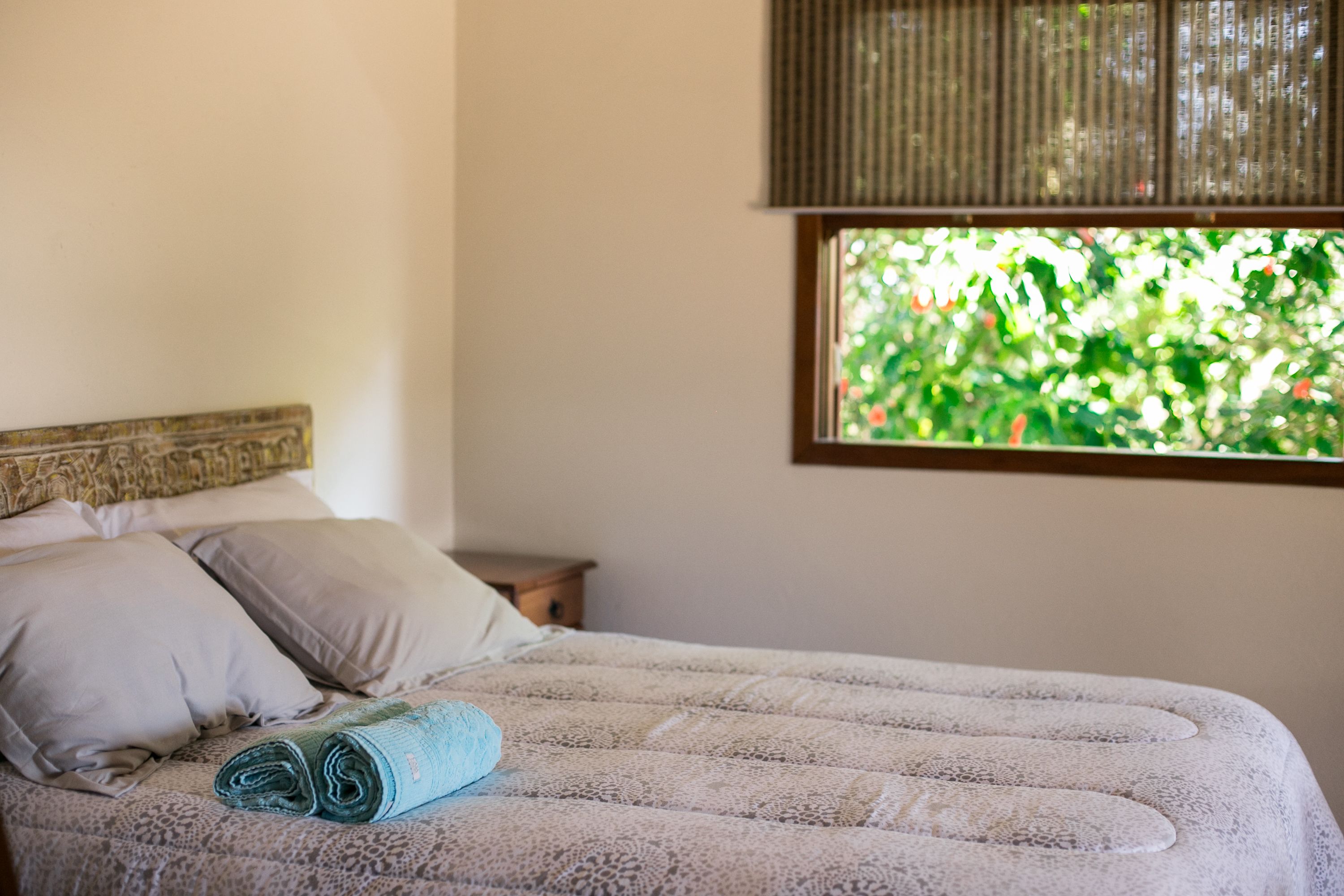 Uma cama com colcha estampada, travesseiros e uma toalha enrolada.