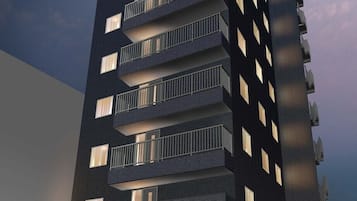 Um edifício moderno alto com várias varandas, entrada no nível da rua e um carro estacionado na frente.