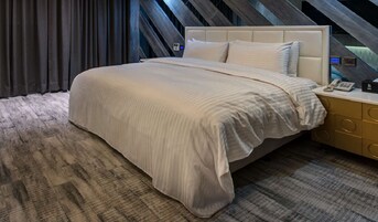 Quarto de hotel moderno com uma cama grande, uma mesa de cabeceira com telefone e painel de controle fixado na parede.