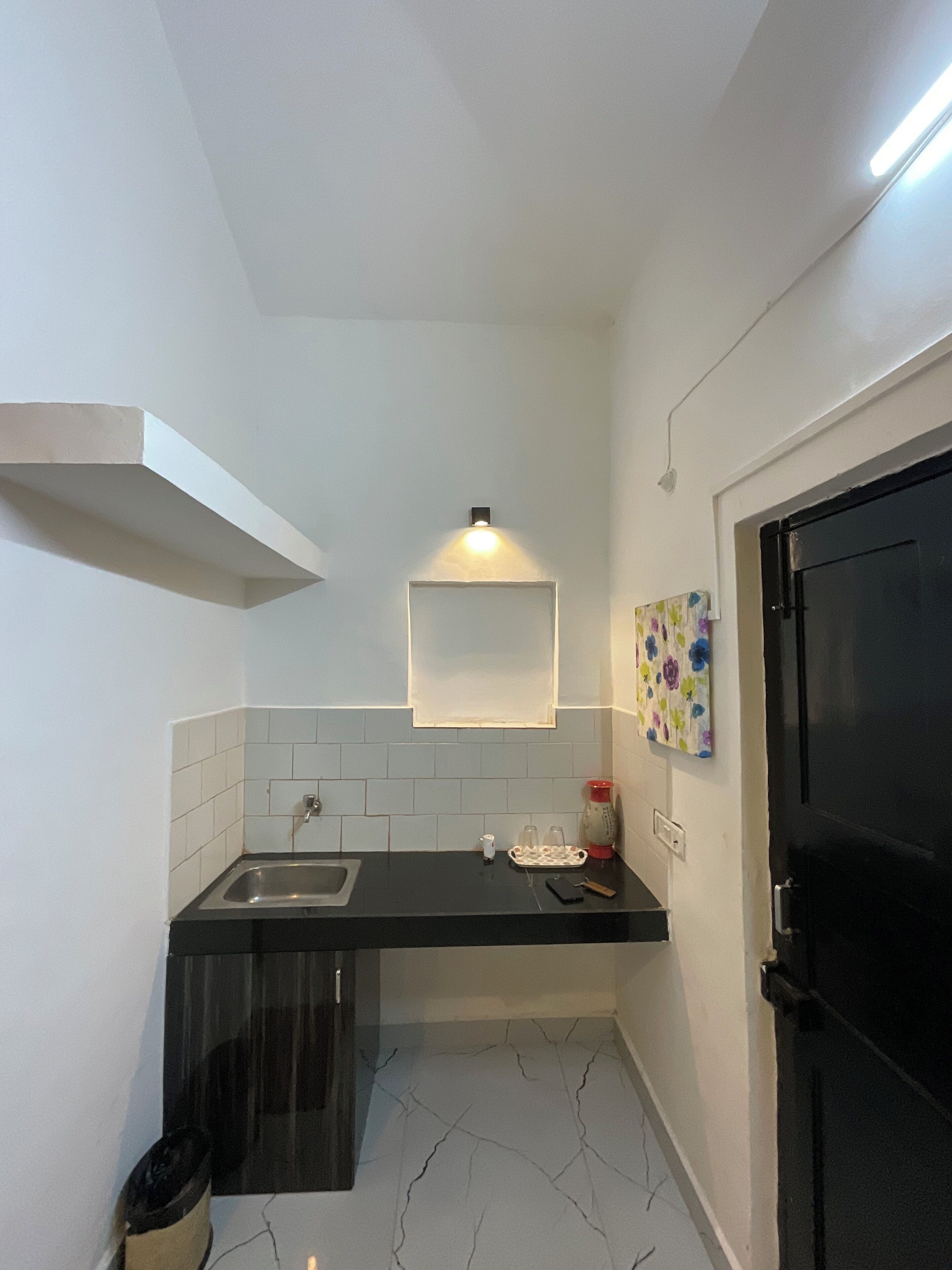 Uma cozinha compacta com bancada preta, azulejos brancos, painel de proteção branco, geladeira preta e uma pia pequena.