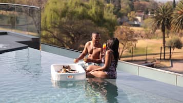 Um casal sentado à beira da piscina com bebidas e petiscos.