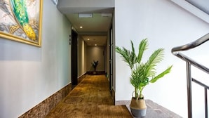 Um corredor com piso de madeira, um vaso com planta, uma obra de arte emoldurada e uma escada.