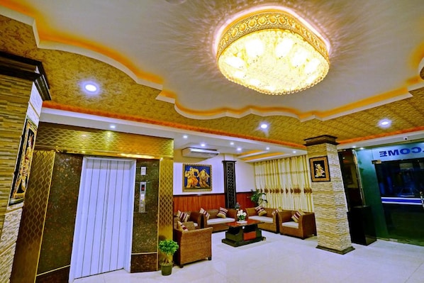 Um hall com lustre, sofás, balcão de recepção e uma parede com pintura.