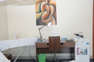 Quarto com escrivaninha, tábua de passar, cadeira e geladeira.