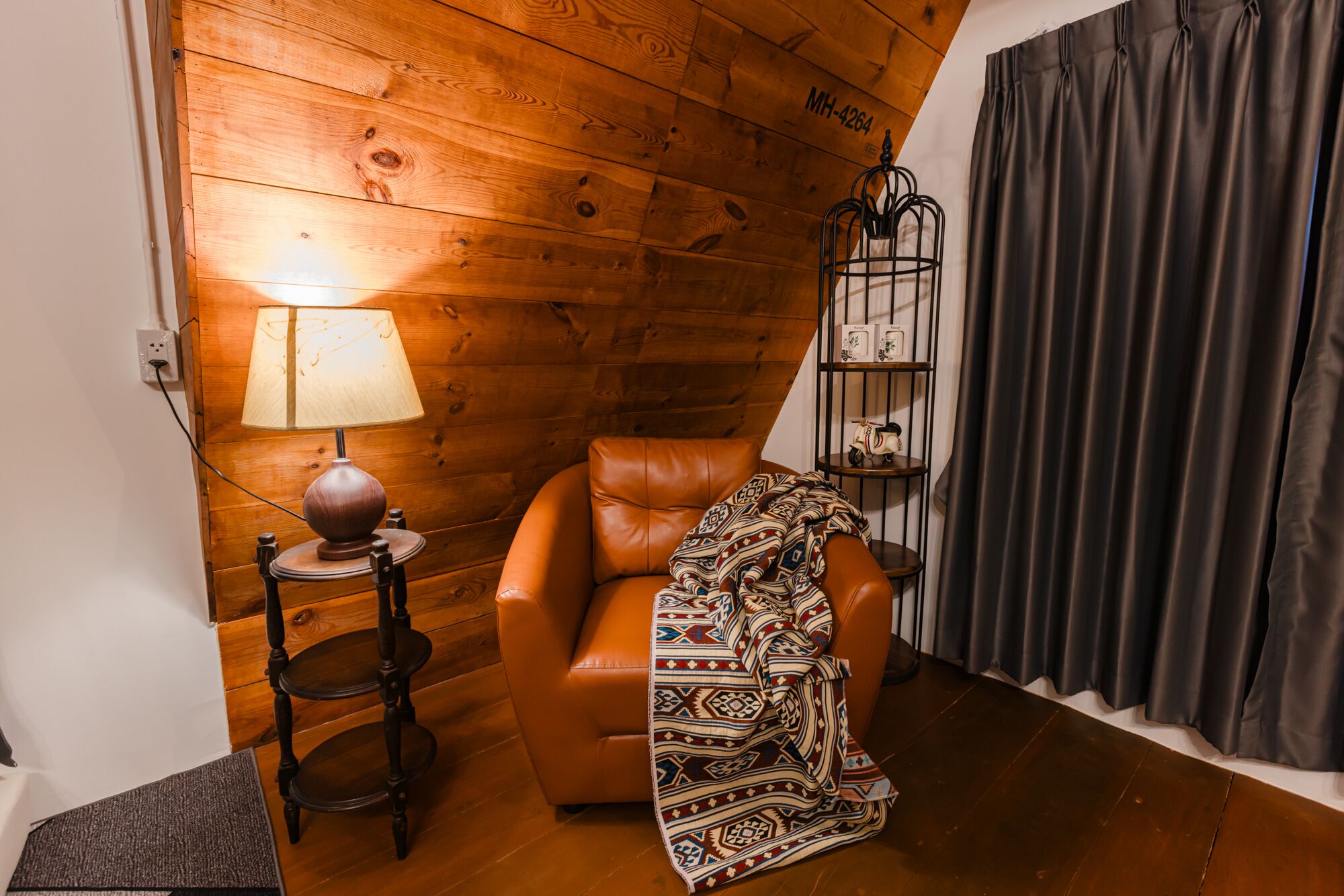 Um quarto aconchegante com uma poltrona de couro, um cobertor estampado, uma luminária e uma prateleira com objetos decorativos.
