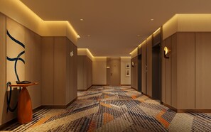 Corredor de hotel com painéis de madeira, carpete estampado e balcão de recepção com telefone.