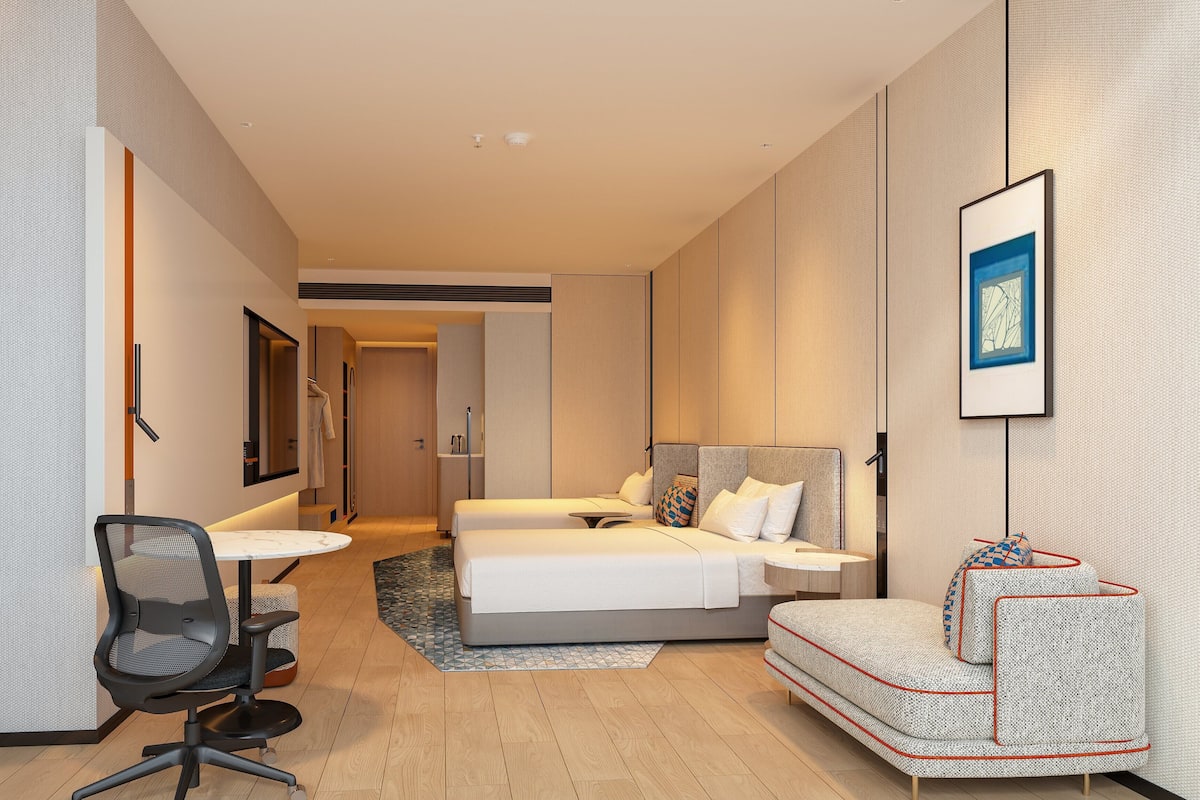 Quarto de hotel moderno com cama, escrivaninha, cadeira e uma moldura na parede.
