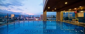 Piscina infinita no terraço com vista para a cidade, pilares xadrez e assentos de lounge modernos.