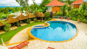 Uma piscina com borda curva, rodeada por espreguiçadeiras e guarda-sóis de palha.
