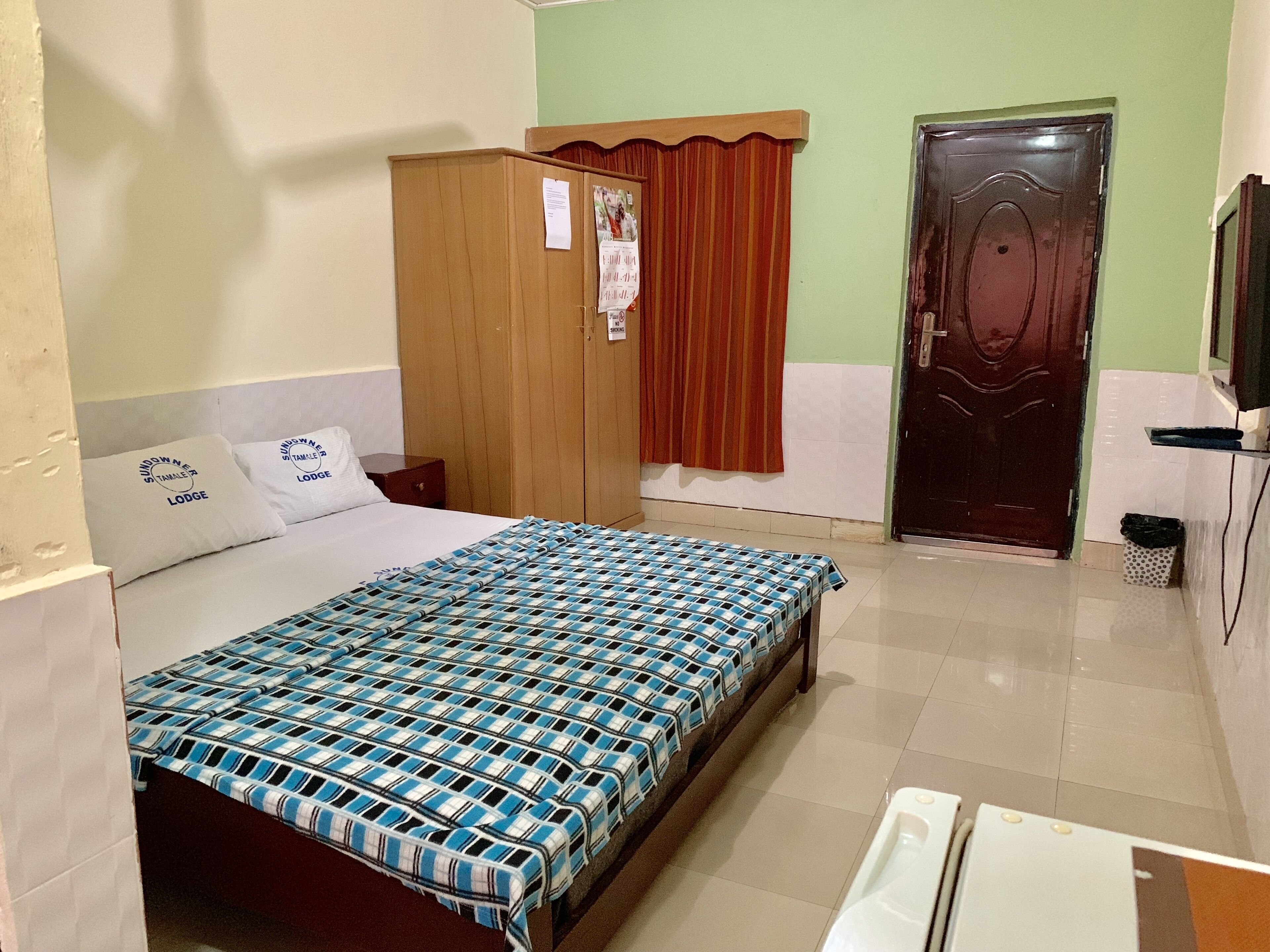Quarto com cama, guarda-roupa de madeira, porta e uma pequena mesa.
