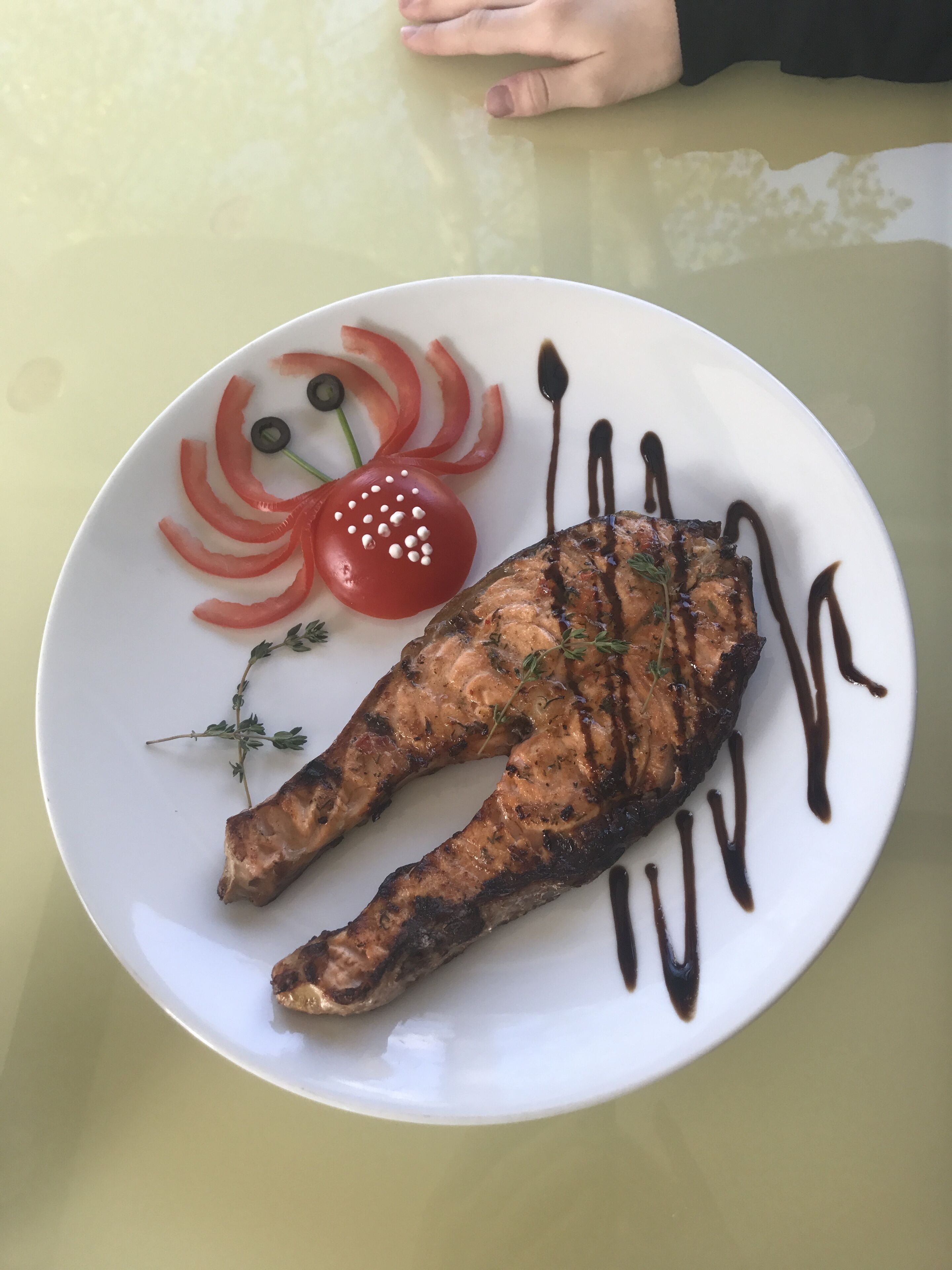 Prato com peixe grelhado, tomate e um enfeite decorativo.