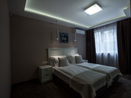 Quarto de hotel com cama de casal, mesa de cabeceira, ar condicionado, luminária no teto e janela com cortinas.