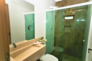 Casa de banho com chuveiro em cabine de vidro, lavatório com espelho e sanita.