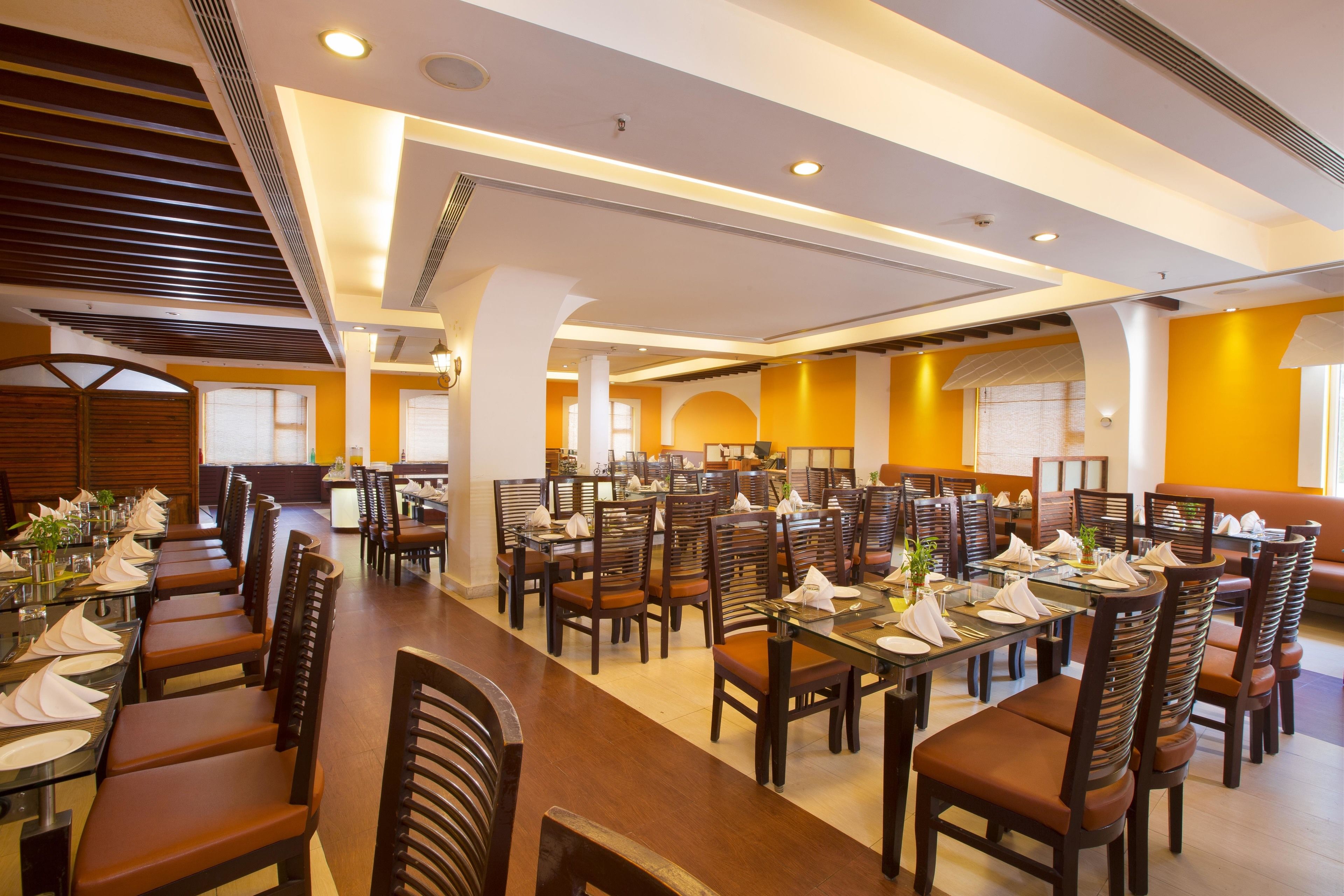 Uma sala de jantar espaçosa com várias mesas e cadeiras, tetos altos com iluminação embutida e um design arquitetônico moderno.