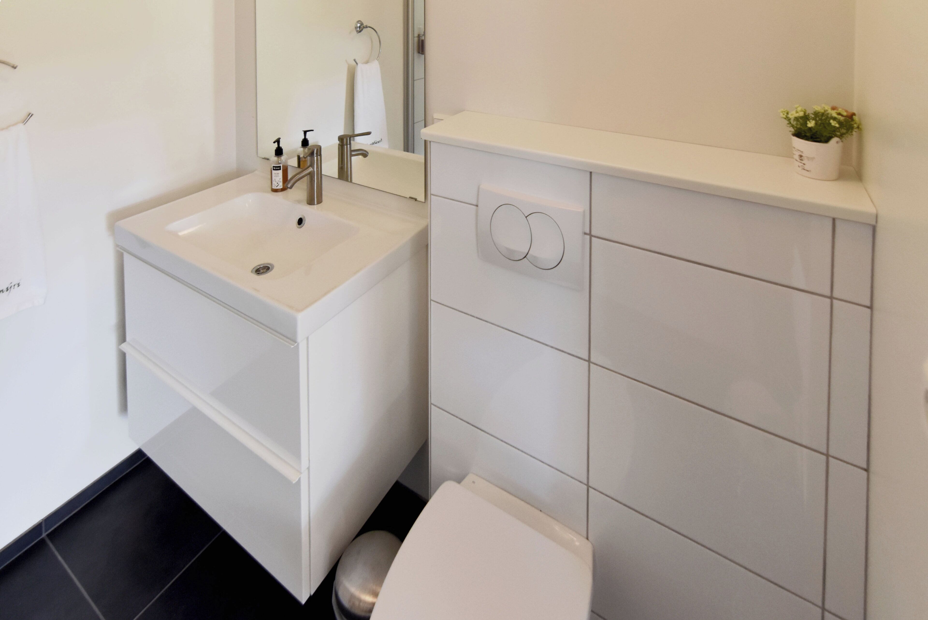 Casa de banho moderna com lavatório branco, espelho e sanita.
