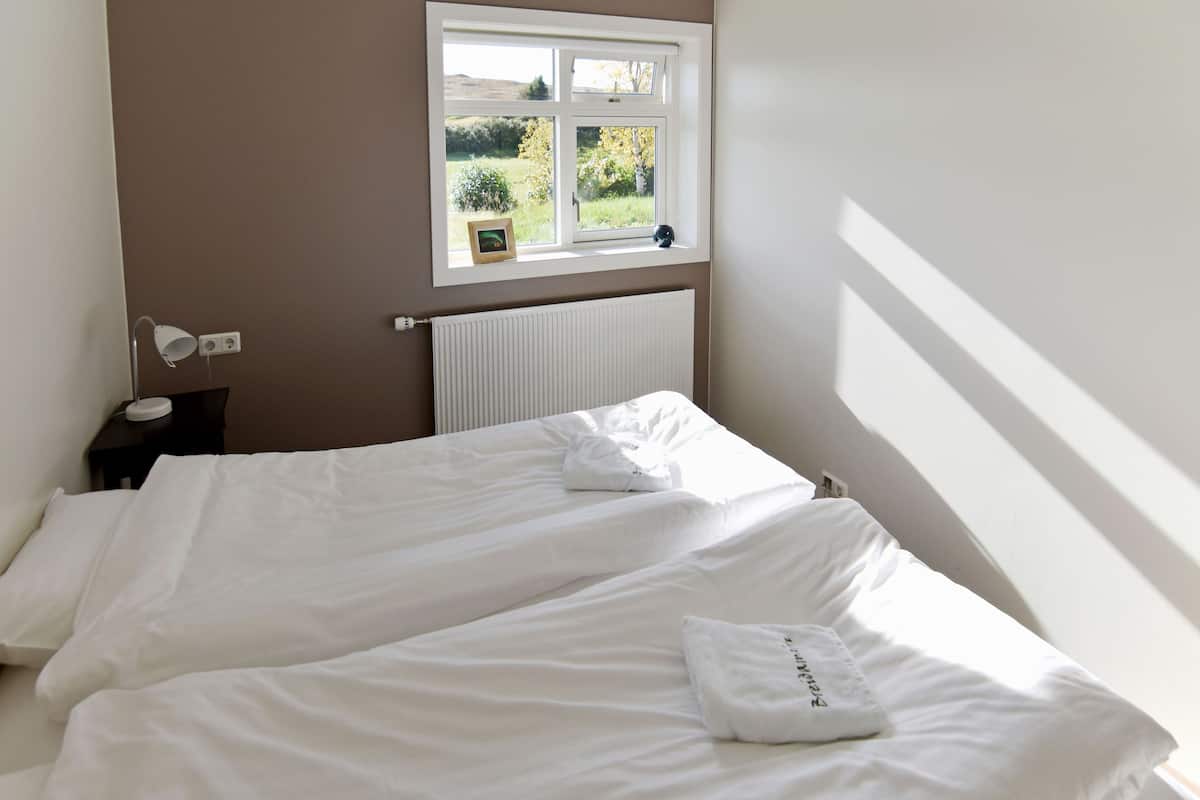 Quarto com duas camas, janela com vista para o verde, abajur e radiador.