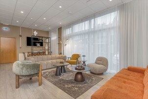 Uma sala de estar moderna com um sofá de canto, poltronas, uma mesa de centro e uma área de jantar com mesa e cadeiras.