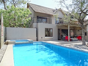 Uma casa moderna com piscina, varanda coberta e escadaria para um andar superior.