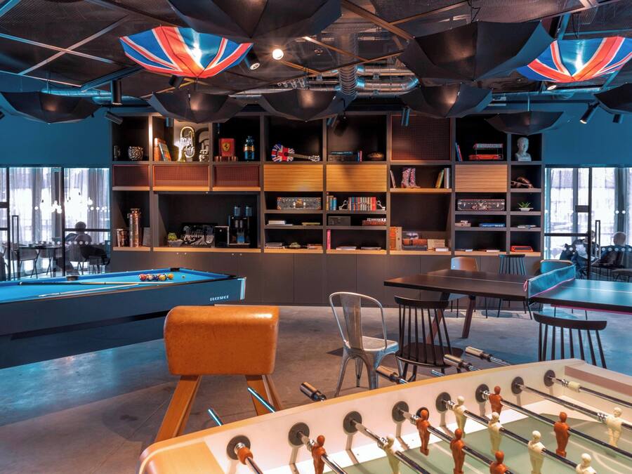 Uma área de lounge moderna com mesa de bilhar, mesa de futebol de mesa e um bar com estantes de livros e objetos de coleção.