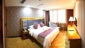 Quarto de hotel com uma cama grande, uma mesa de cabeceira com luminária, uma cadeira e uma escrivaninha com luminária.