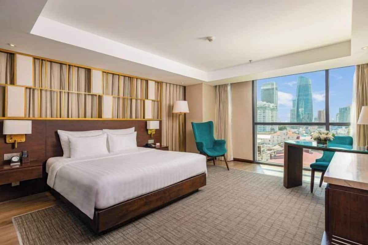 Quarto de hotel com uma cama grande, uma escrivaninha, uma cadeira e vista para a cidade.