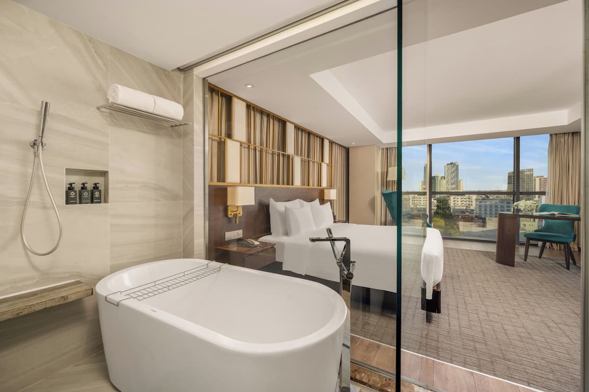 Quarto de hotel moderno com banheira, cama, escrivaninha e varanda com vista para a cidade.