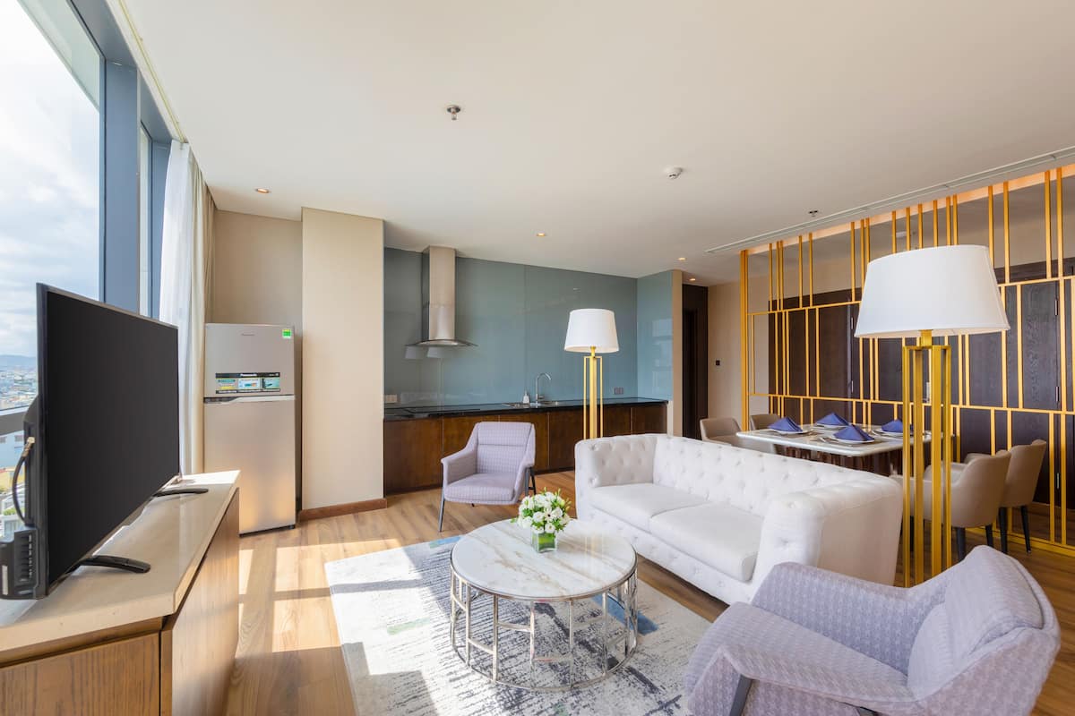 Quarto de hotel moderno com uma televisão grande, um sofá, um espaço de refeições e uma cozinha.