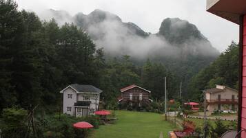 Um ambiente rural com gramado, um guarda-sol vermelho e um edifício com varanda.