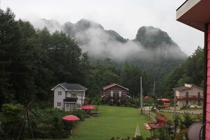 Um ambiente rural com gramado, um guarda-sol vermelho e um edifício com varanda.