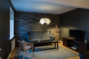 Uma sala de estar moderna com um sofá cinza escuro, uma mesa de centro, uma televisão sobre um suporte de madeira e uma luminária pendente única.