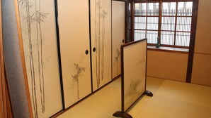 Um quarto japonês tradicional com tatames, portas deslizantes shoji com detalhes em bambu e vista através de uma divisória shoji.