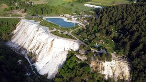 Vista aérea de um resort com um penhasco imponente, uma piscina e uma área arborizada.