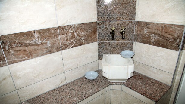 Casa de banho com canto, parede de mármore, bancada de granito, lavatório branco e duas torneiras.