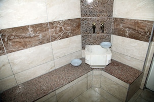 Casa de banho com canto, parede de mármore, bancada de granito, lavatório branco e duas torneiras.