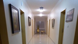 Um corredor com piso de azulejos, portas em ambos os lados e quadros nas paredes.