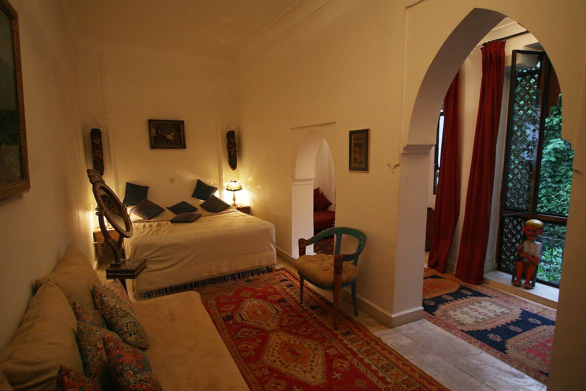 Quarto com cama, cadeira, tapete e janela com cortinas.