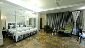 Quarto com cama de dossel, uma cadeira, mesinha e uma janela grande com cortinas.