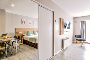 Quarto de hotel moderno com cama, mesa de jantar, cadeiras, televisão e obras de arte na parede.