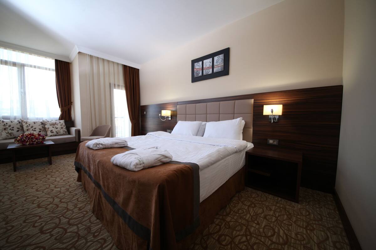Quarto de hotel com uma cama grande, um sofá, uma mesa de centro e uma luminária na parede.