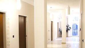 Um corredor de hotel com piso de mármore, paredes brancas e uma porta de madeira.