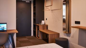 Quarto de hotel moderno com uma cama, uma escrivaninha com um laptop, um banco de madeira, um espelho e um guarda-roupa.