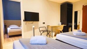 Quarto de hotel com duas camas, uma escrivaninha, uma cadeira, uma televisão e um guarda-roupa.